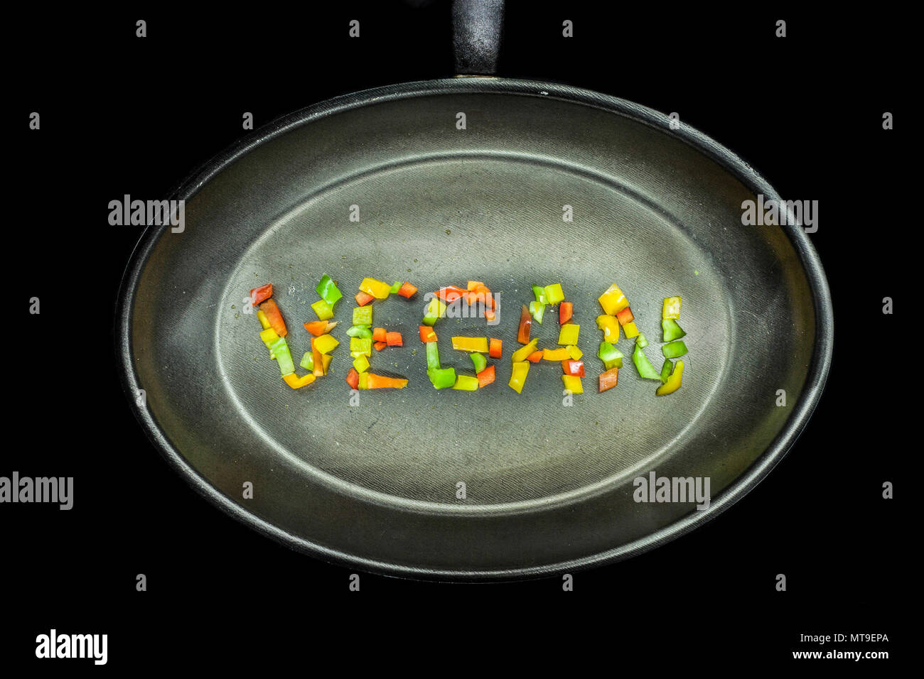 Vegan word written with chopped vegetables on a pan isolated on a black ...