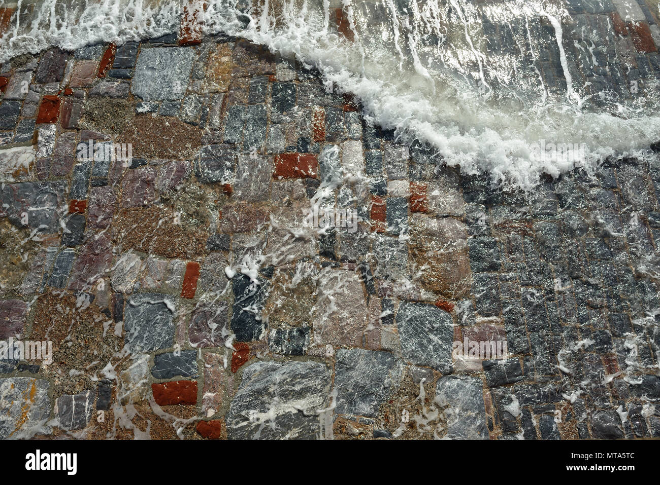 Colourful stones in a ramp along the sea wall being washed by the waves ...