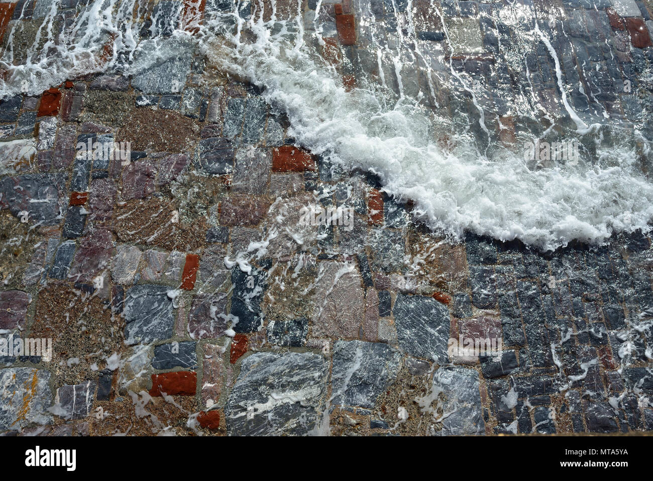 Colourful stones in a ramp along the sea wall being washed by the waves ...