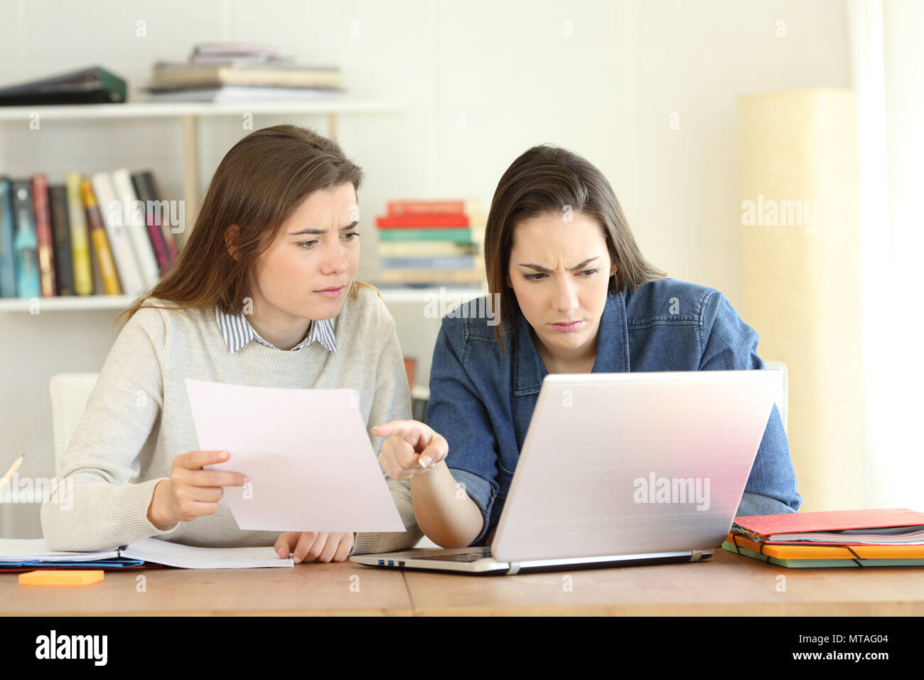 Two concentrated students comparing paper documents online with a ...