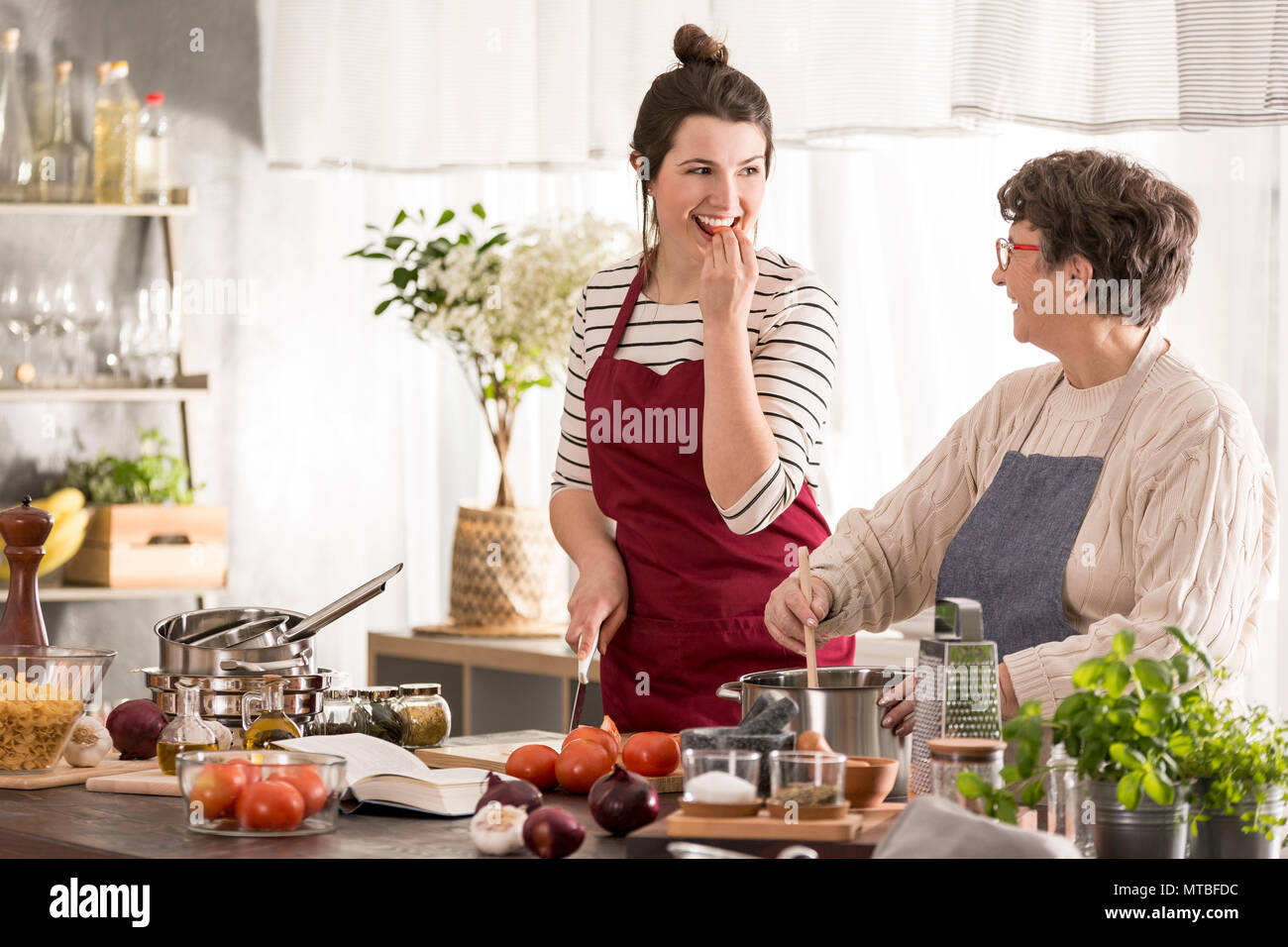 Happy granddaughter looking at her grandma while cooking Stock Photo ...
