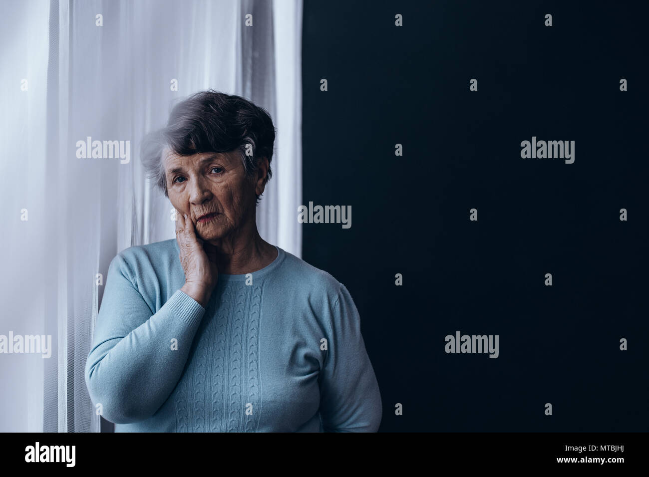 Sad, elderly woman standing alone beside window Stock Photo - Alamy