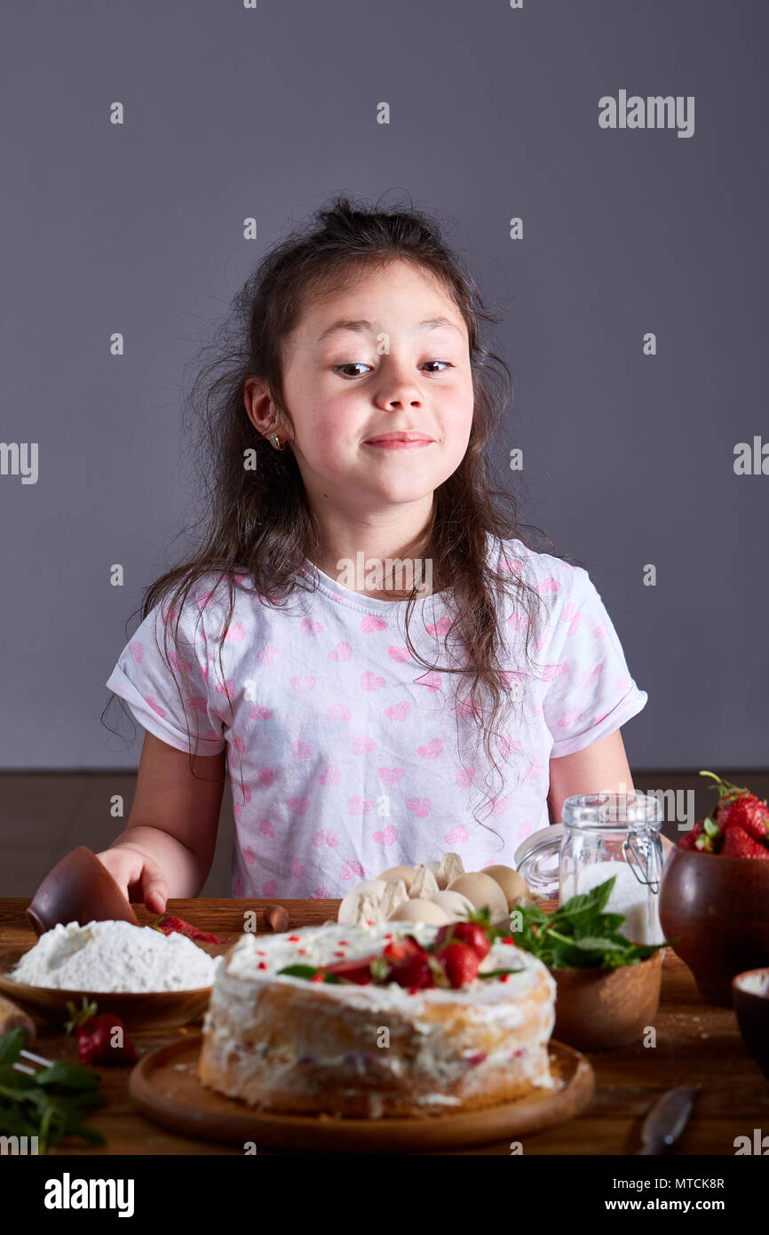 Happy sweet girl in white T-shirt enjoying strawberry cake in a studio ...