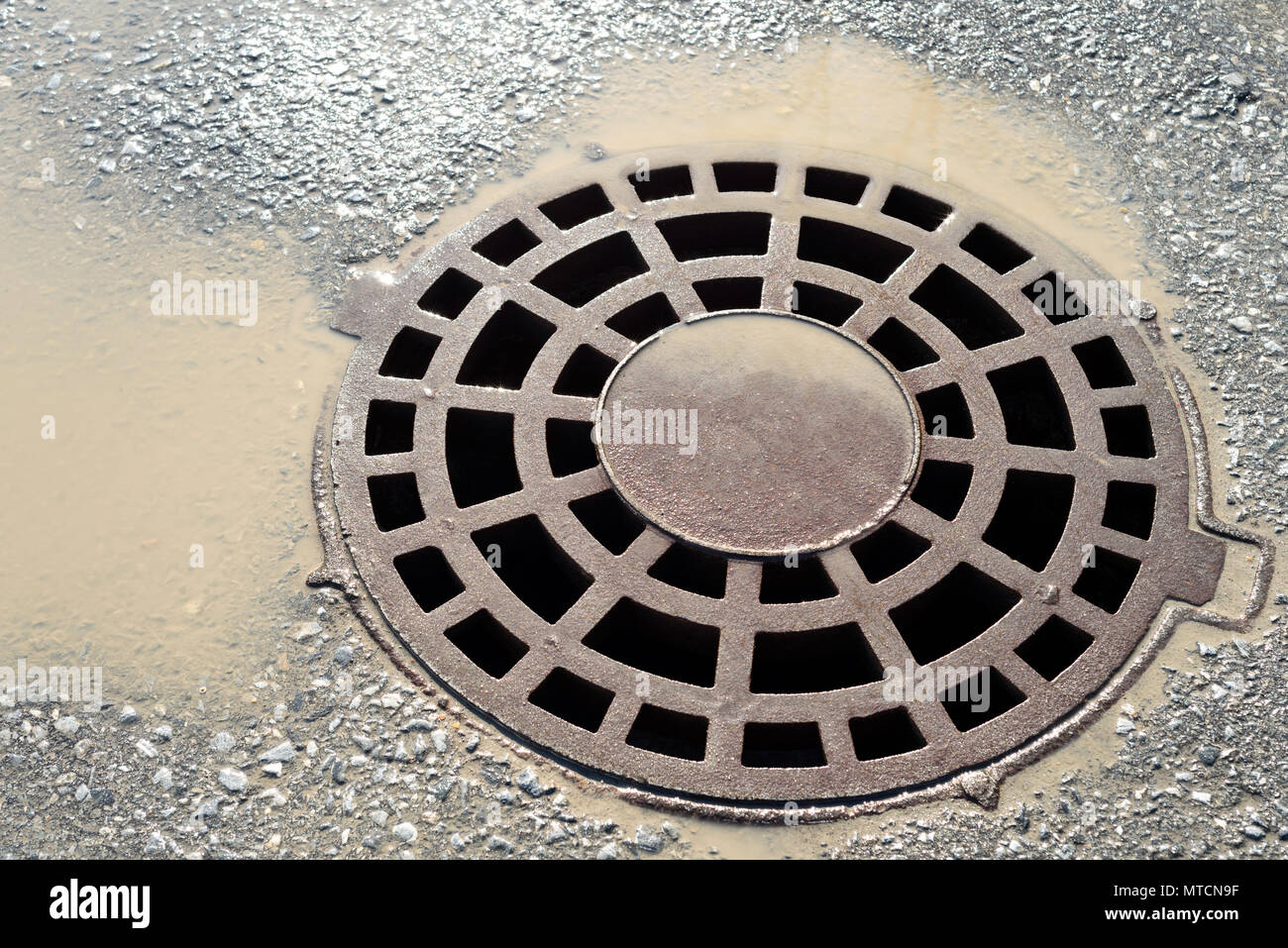 Cast iron metal rain manhole cover in tarmac with fresh mud stained ...
