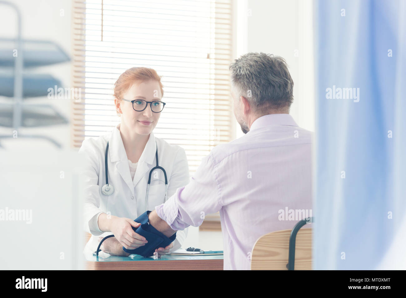 Smiling doctor measuring pressure of sick patient in a hospital Stock ...