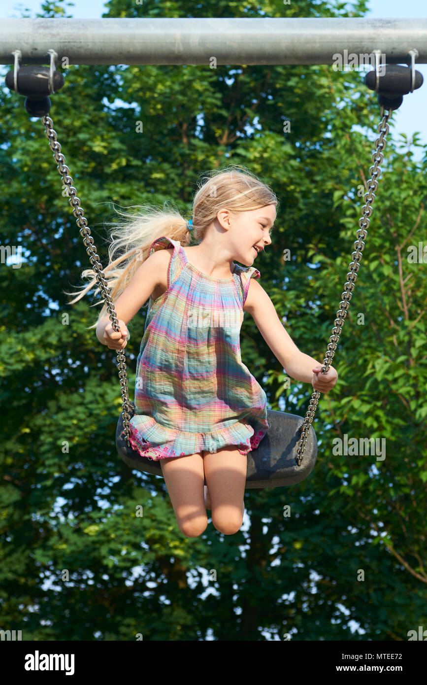 Little child blond girl having fun on a swing outdoor. Summer playground. Girl swinging high ...