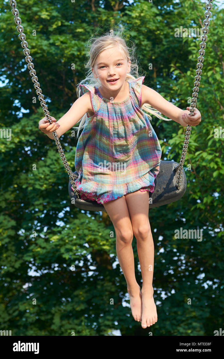 Little child blond girl having fun on a swing outdoor. Summer playground. Girl swinging high ...