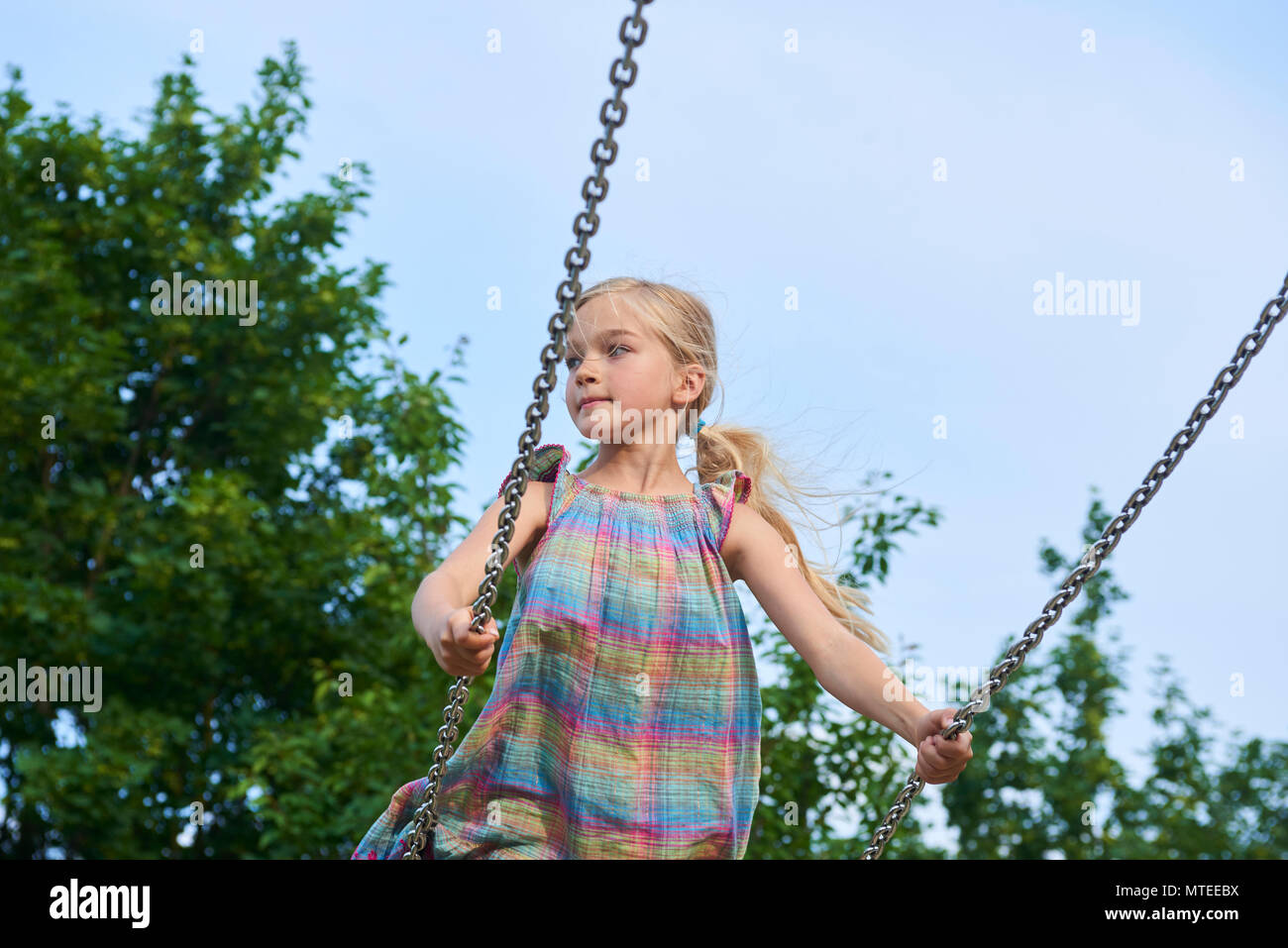 Little child blond girl having fun on a swing outdoor. Summer playground. Girl swinging high ...