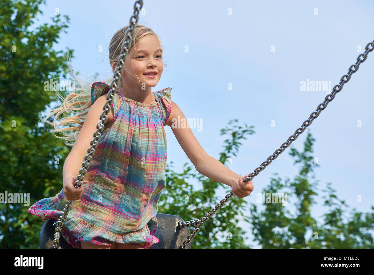 Little child blond girl having fun on a swing outdoor. Summer playground. Girl swinging high ...