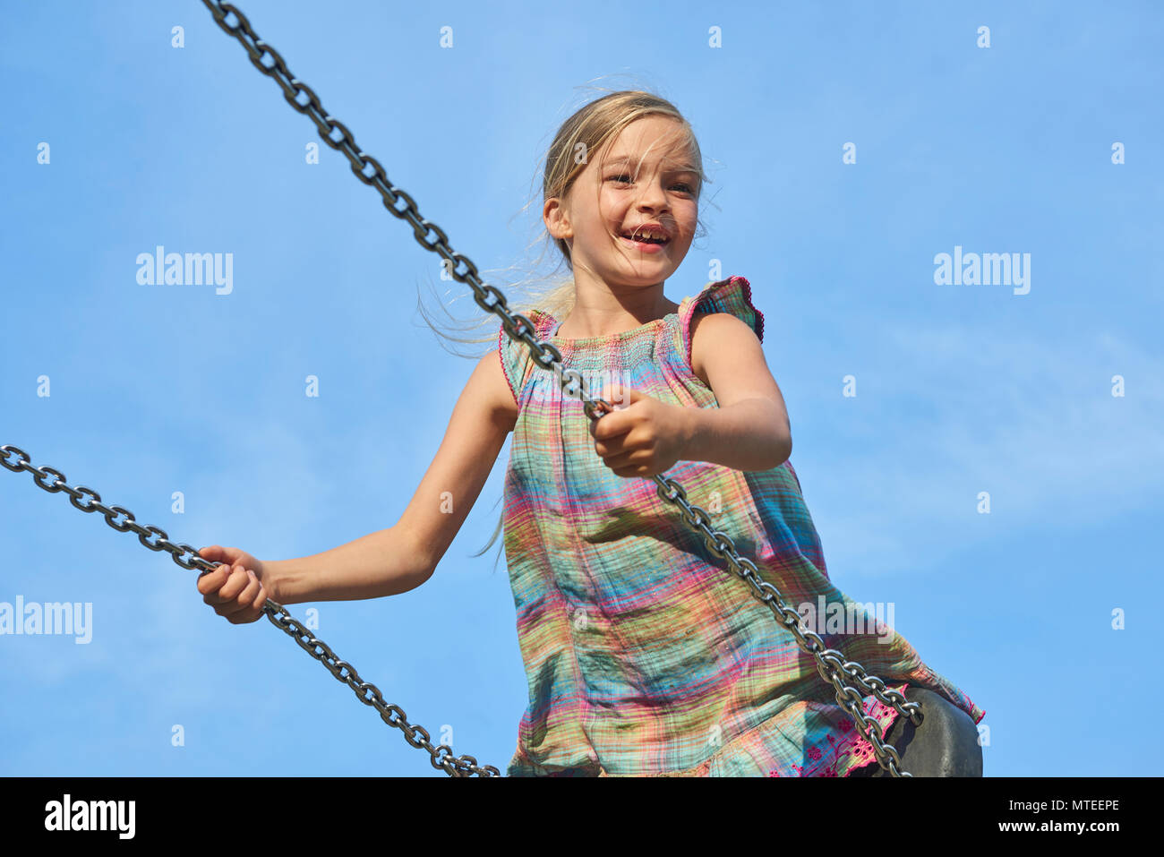Little child blond girl having fun on a swing outdoor. Summer playground. Girl swinging high ...