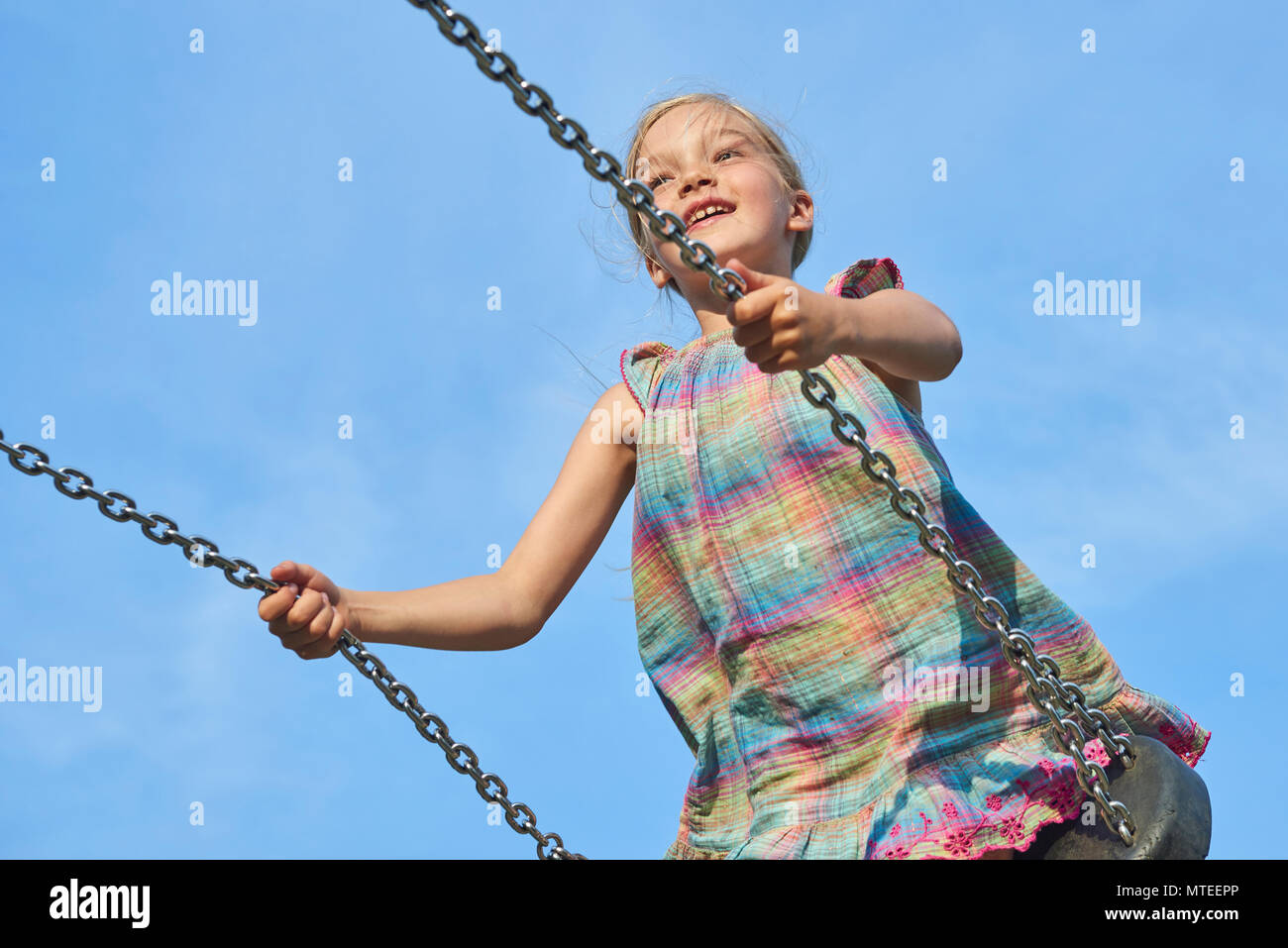 Little child blond girl having fun on a swing outdoor. Summer playground. Girl swinging high ...