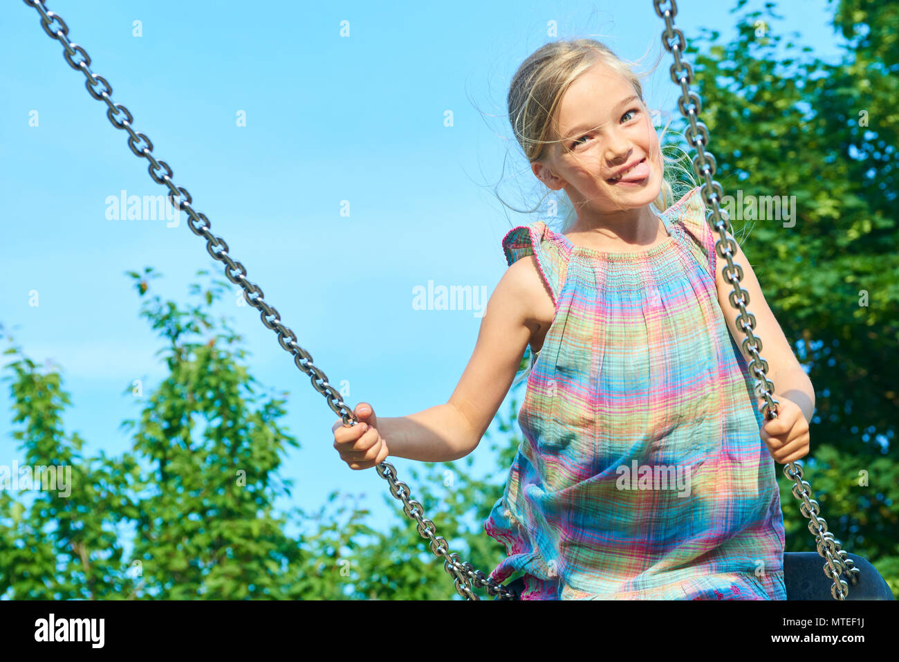 Little child blond girl having fun on a swing outdoor. Summer playground. Girl swinging high ...