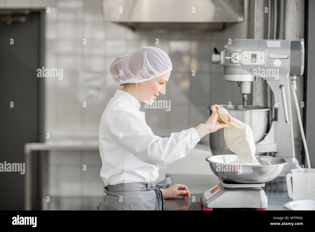Woman confectioner in uniform weighing ingredients for pastry working ...