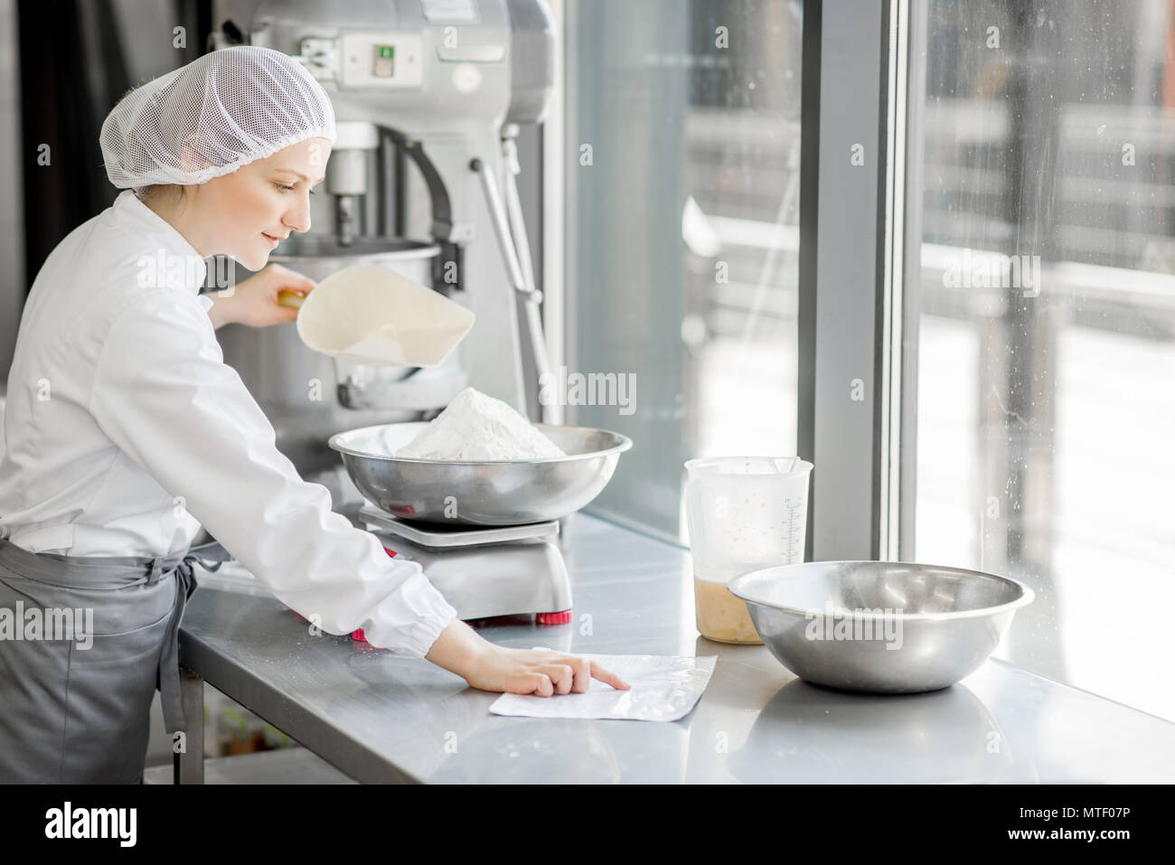 Woman confectioner in uniform weighing ingredients for pastry working ...