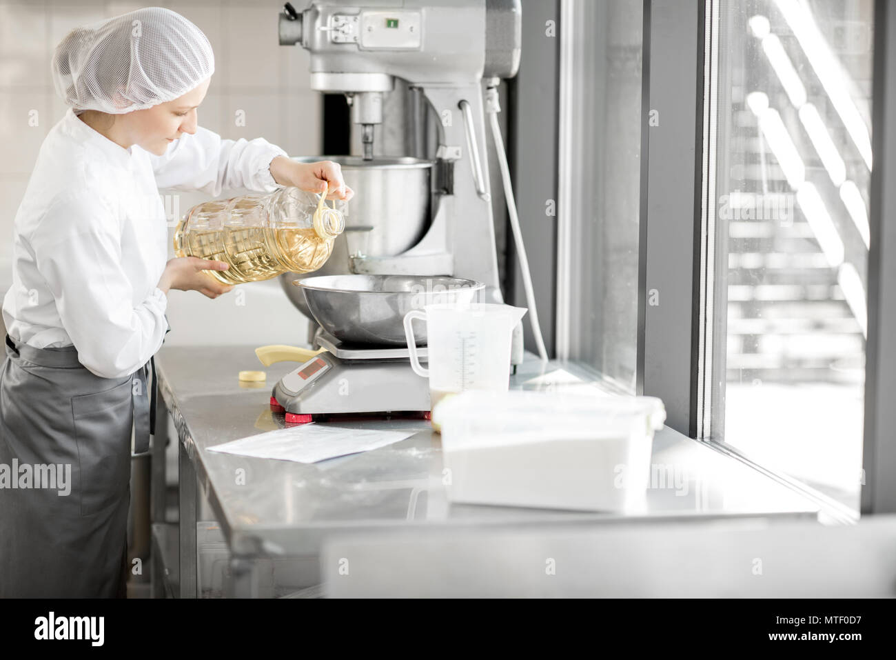Woman confectioner in uniform weighing ingredients for pastry working ...