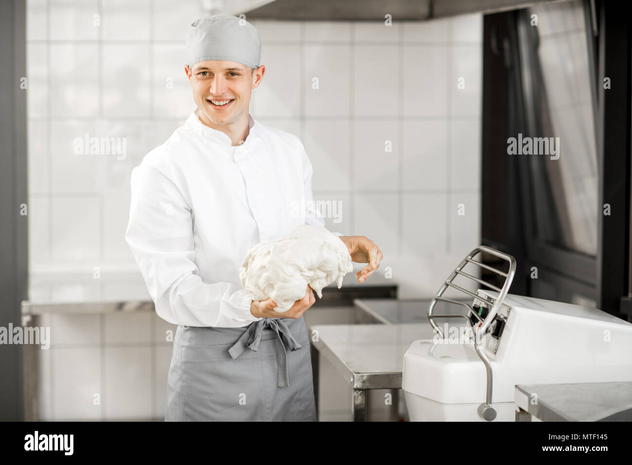 Portrait of a male baker mixing dough with professional kneader machine ...