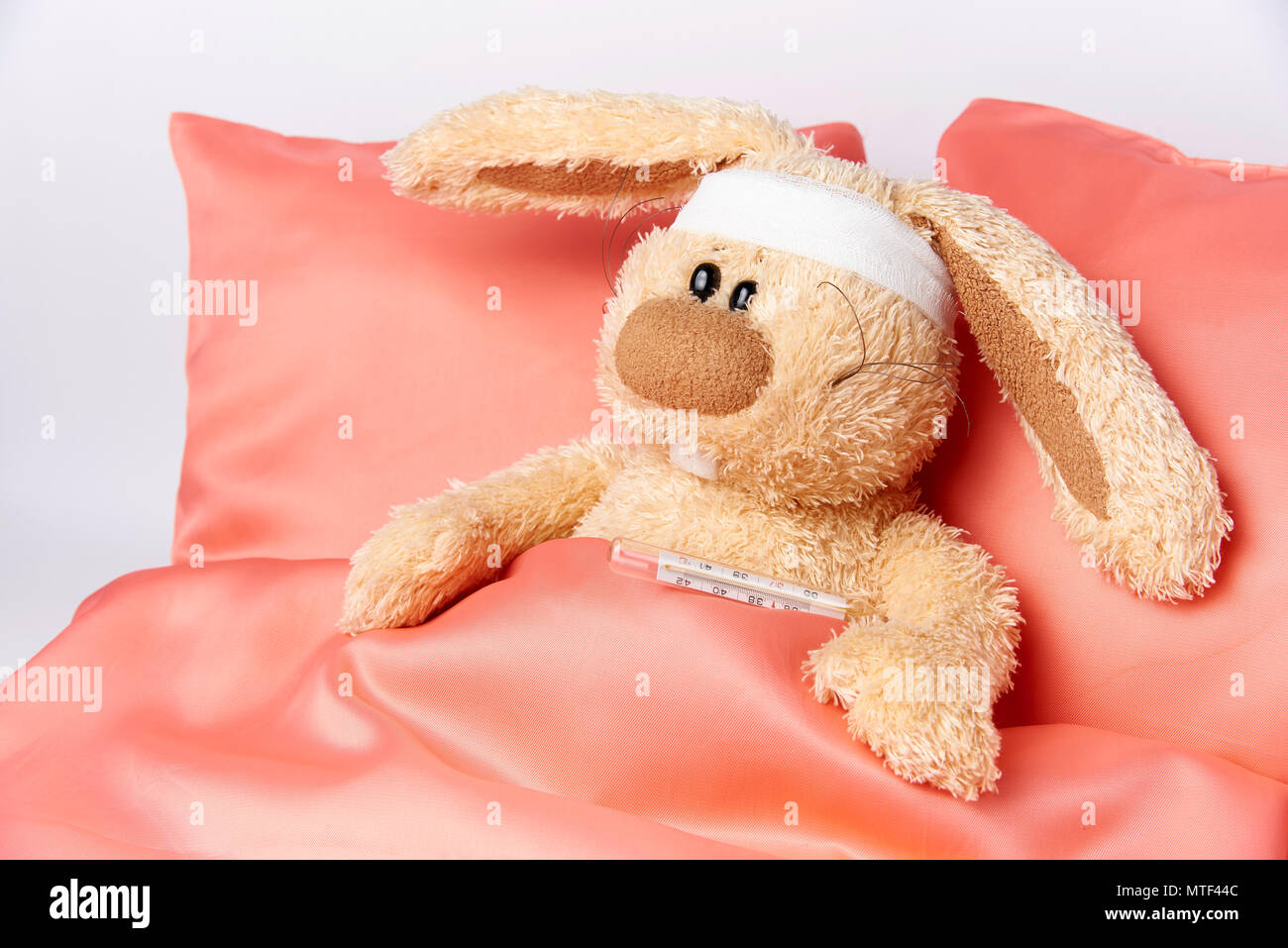Toy unhealthy rabbit with a bandaged head and with a thermometer lies ...
