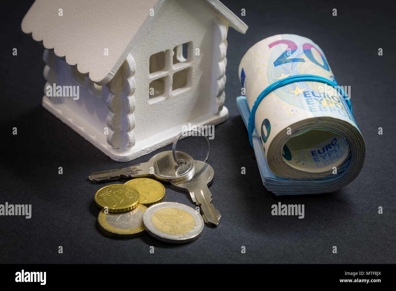 A mock-up house of white color, keys, a roll consisting of money, coins ...