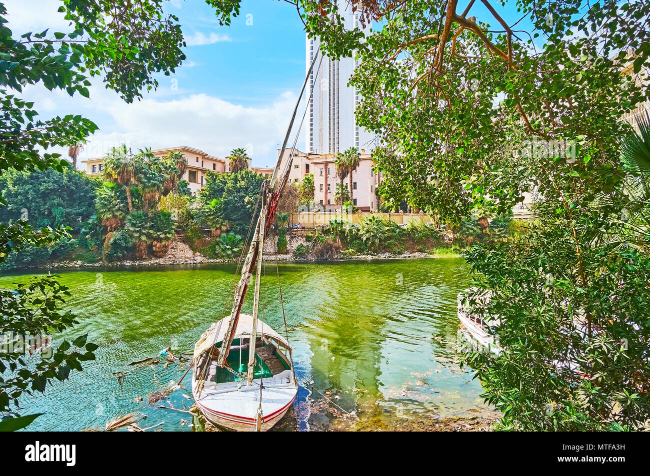 The view on old felucca through the lush trees of riverside garden ...