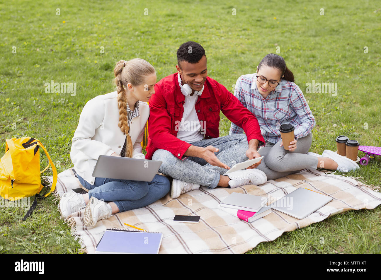 Three good-looking students sitting in the park near university Stock ...