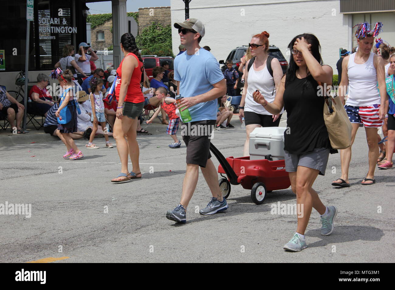 Small town scene of people walking in the parade and a man pulling a ...