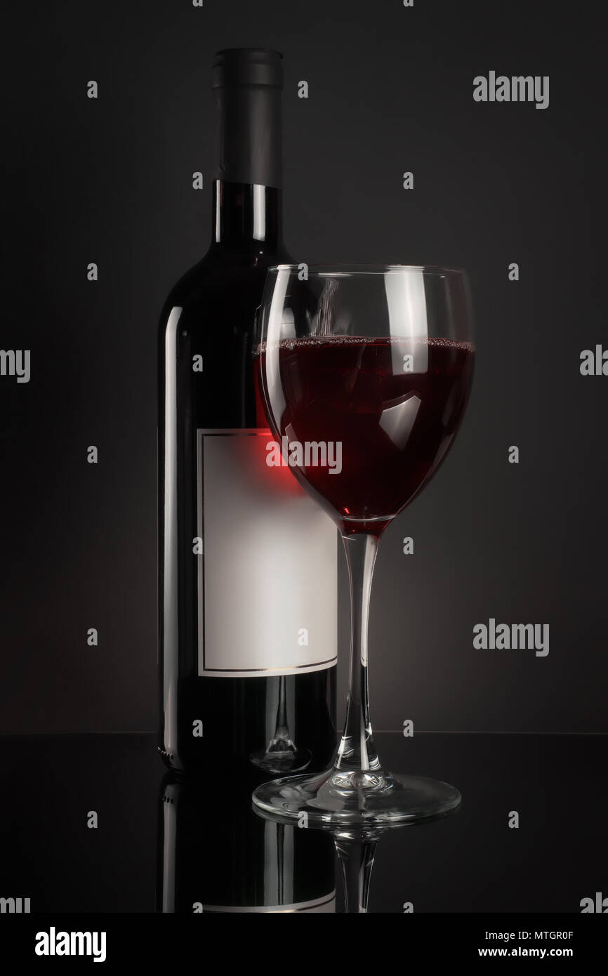 Red wine bottle with blank label and full wineglass. On black ...
