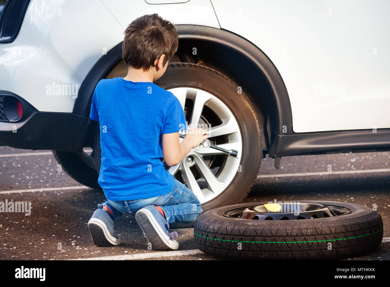 Back view portrait of little boy learning how to change flat tyre using ...