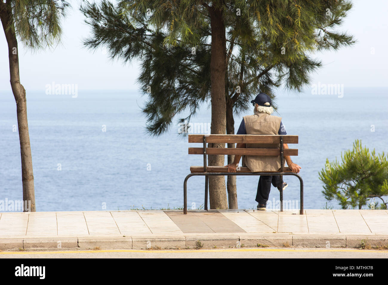 An elderly man sits on a bench by the sea and looks into the distance ...