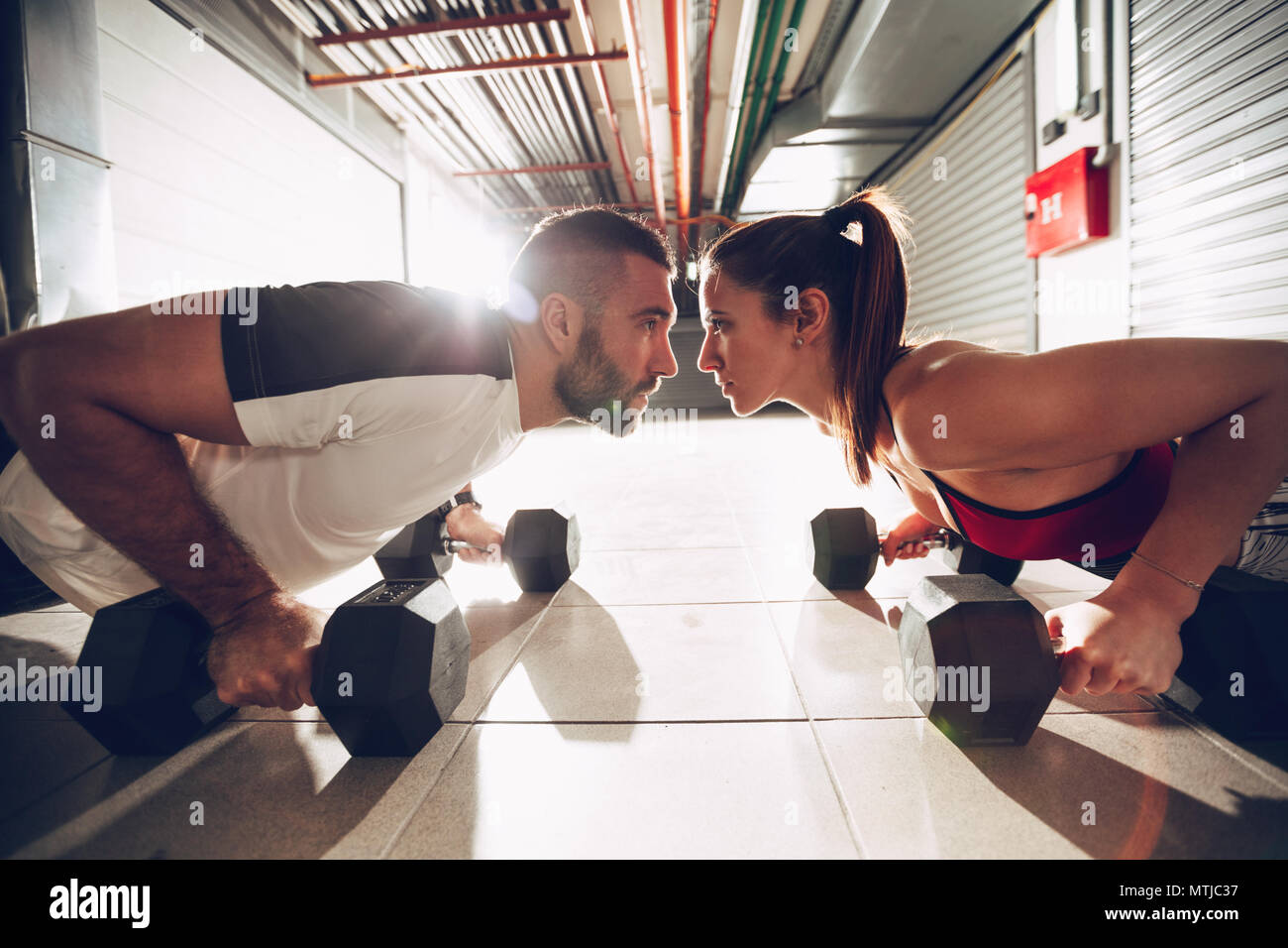 Young muscular couple doing push-up exercise with dumbells on hard ...