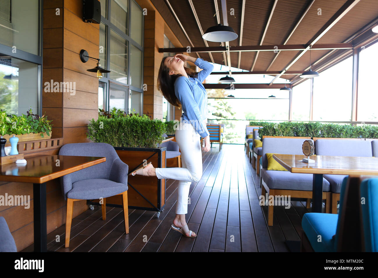Female photo model standing near tables at cafe and keeping smartphone ...