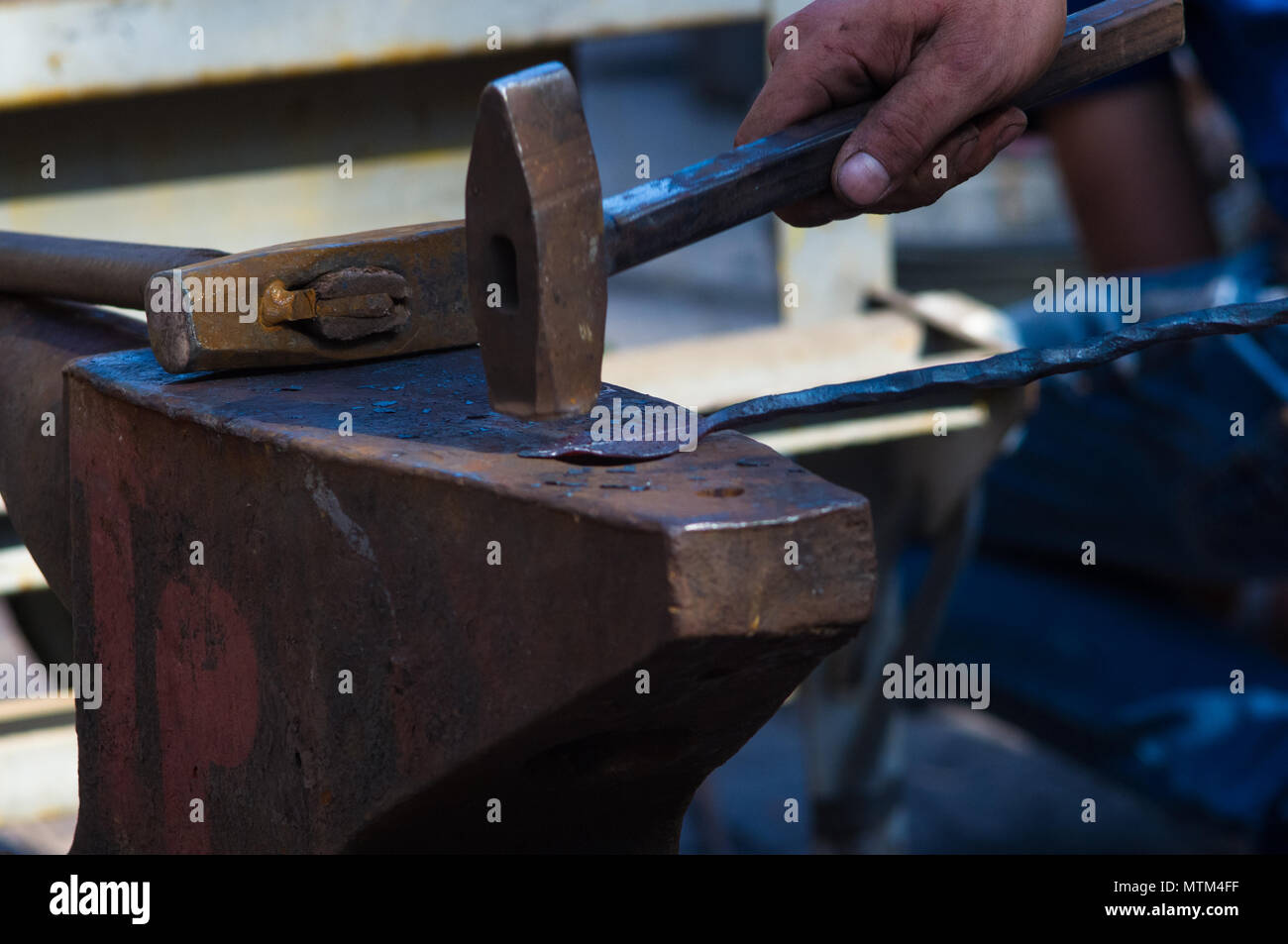 blacksmith performs the forging of hot glowing metal on the anvil ...