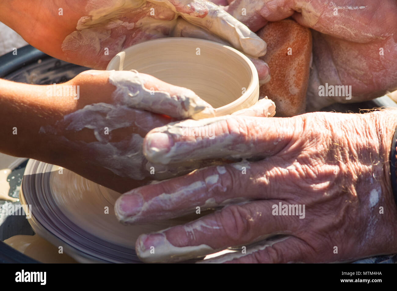 adult hand fed baby's hands to work with a potter's wheel, close up ...