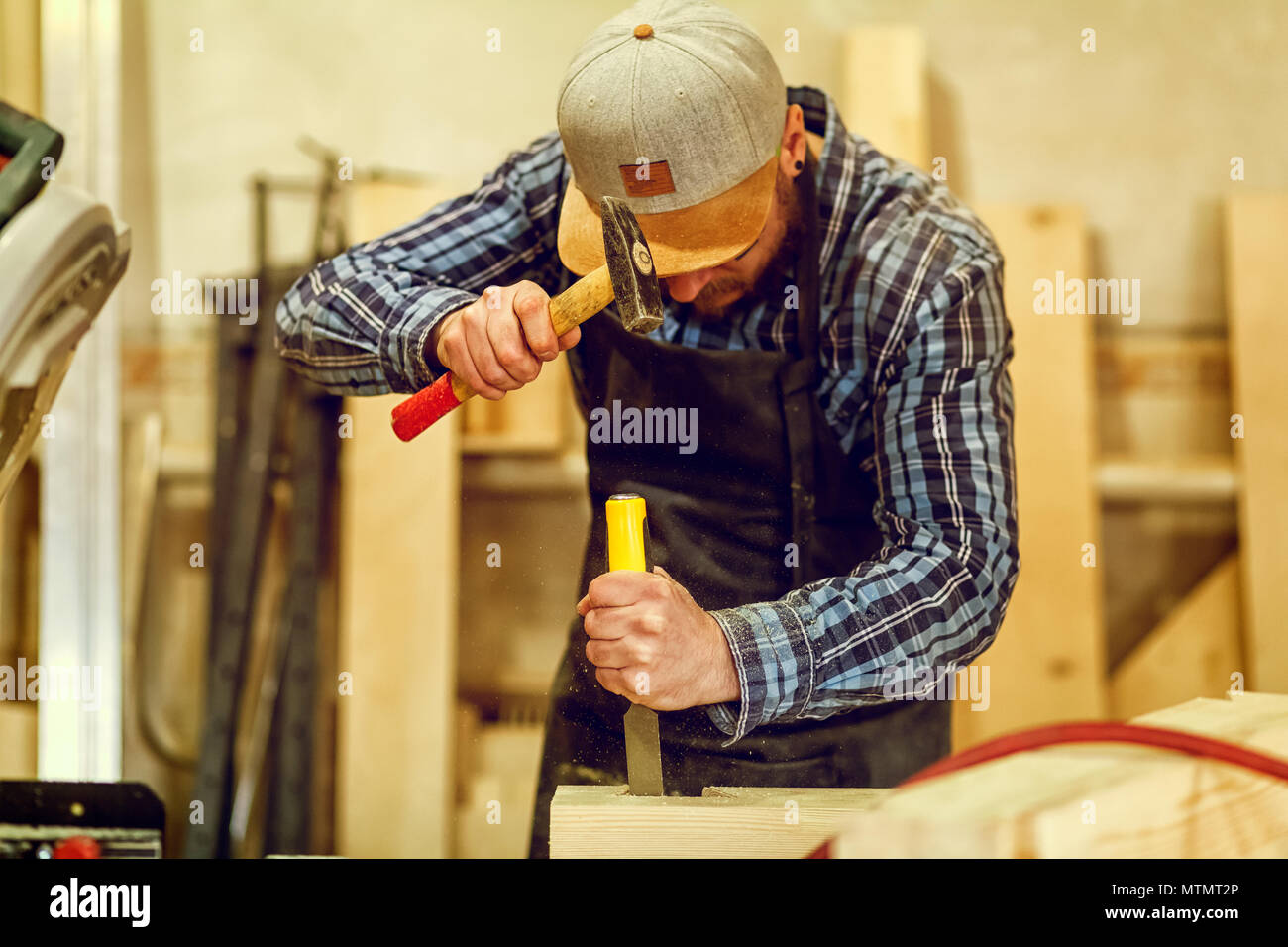 Strong carpenter in work clothes carving wood using a woodworking tool ...