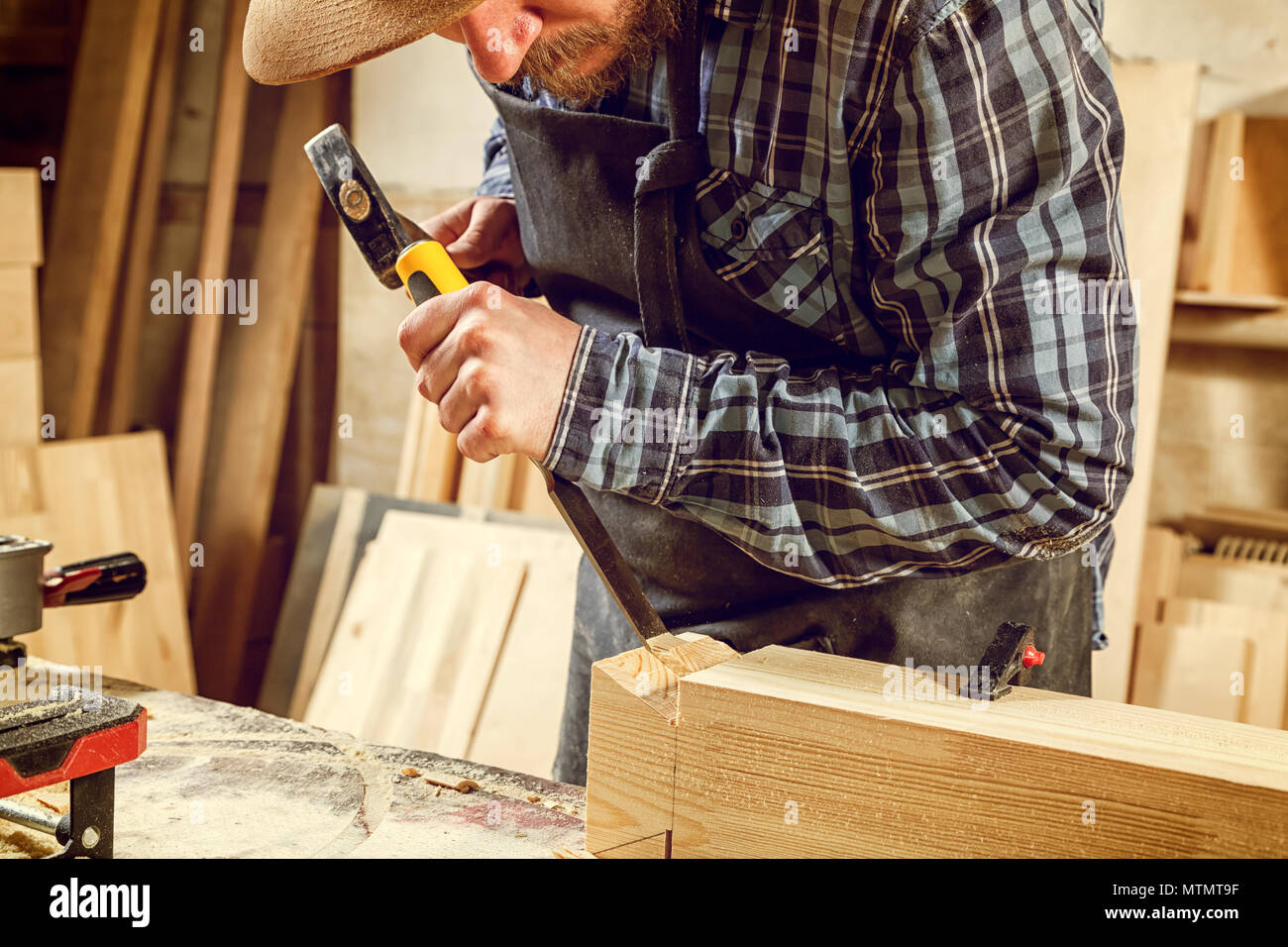 Strong carpenter in work clothes carving wood using a woodworking tool ...