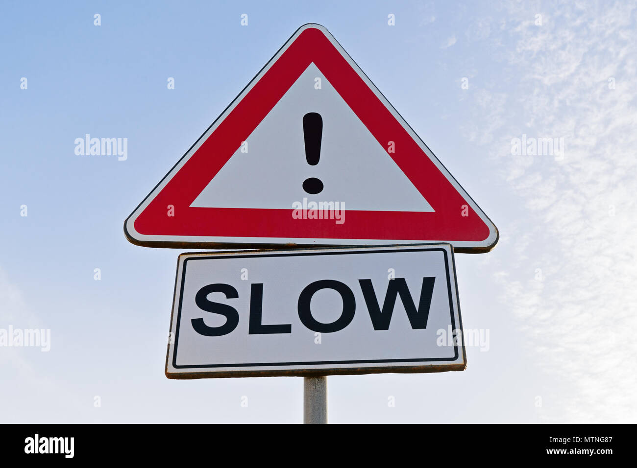 Red and white attention warning road sign "SLOW" against blue sky ...