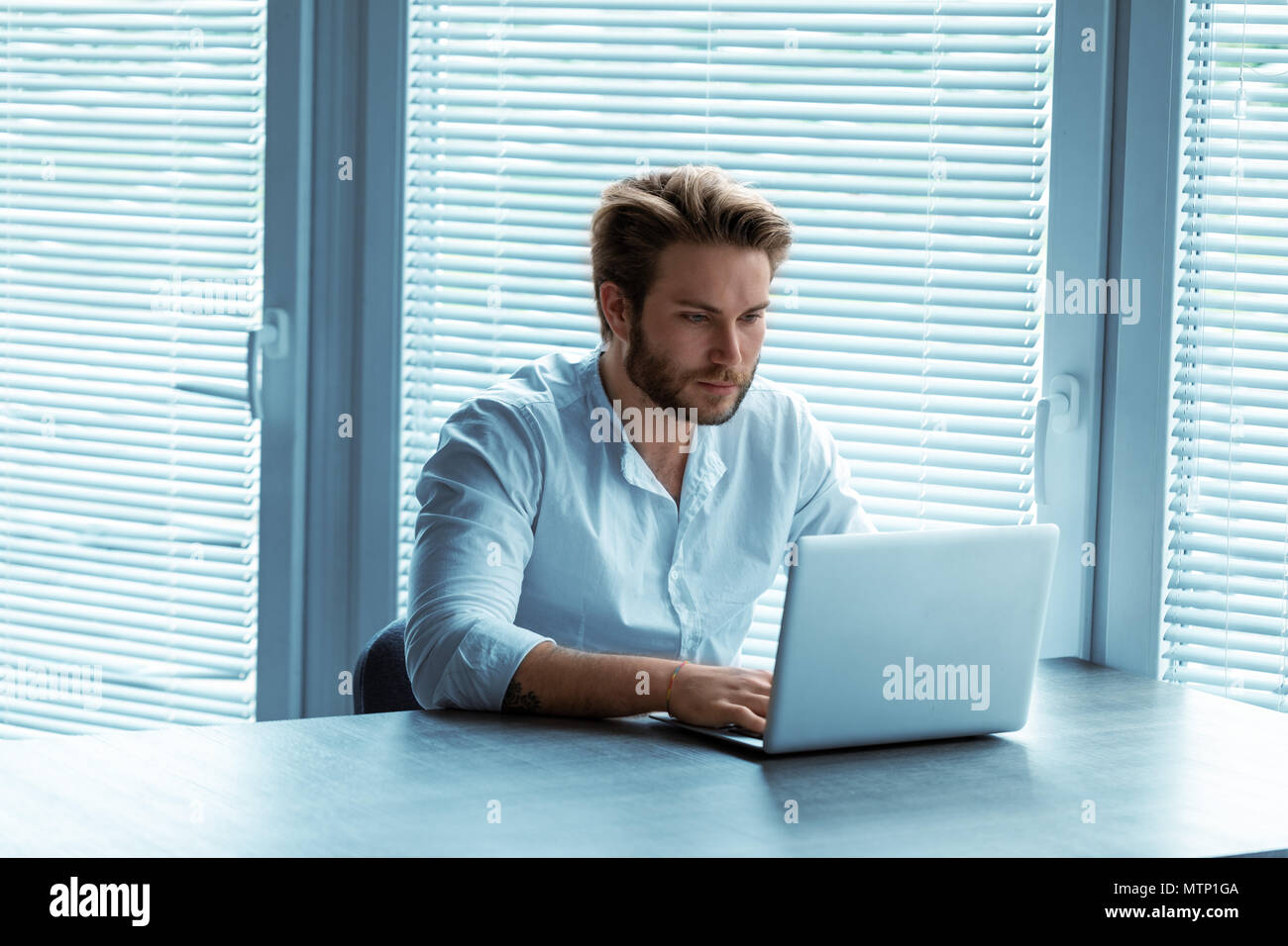 Attractive man sitting working at a laptop computer at an office table ...