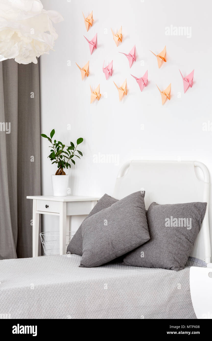 Part of bright room with grey bedding on the bed and paper origami ...