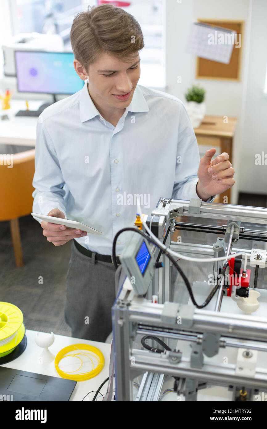Cheerful young man practicing at using 3D printer Stock Photo - Alamy