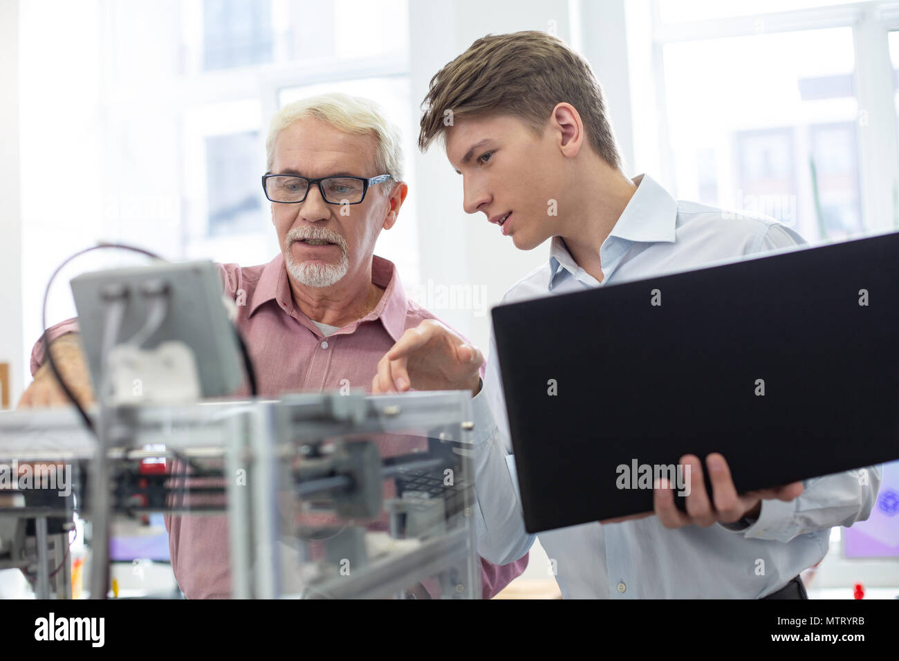 Charming young intern and his supervisor using 3D printer together ...