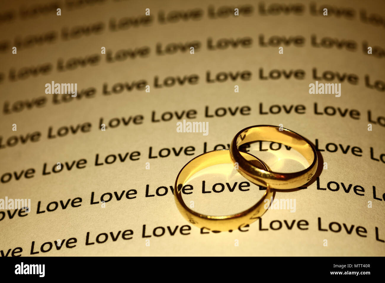 Gold wedding rings on an open book with the word love repeated on the ...
