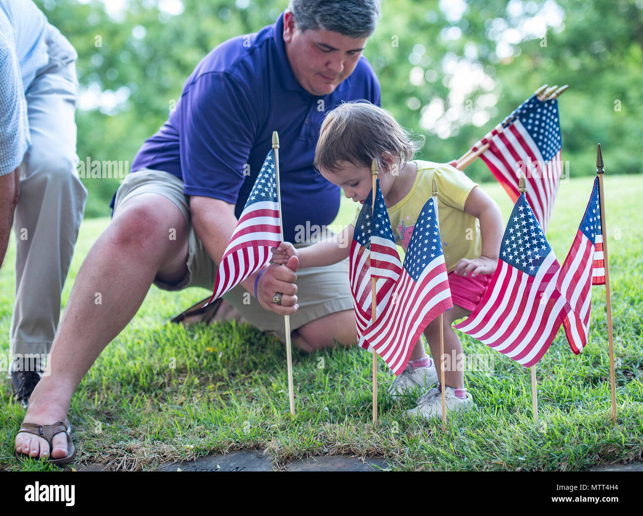 Pastor Gene Aiken helps Teagen Lambert, 2, place an American flag on ...