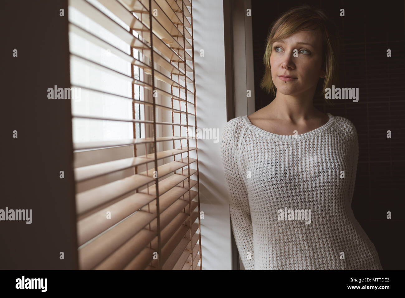 Woman looking through window blind Stock Photo - Alamy