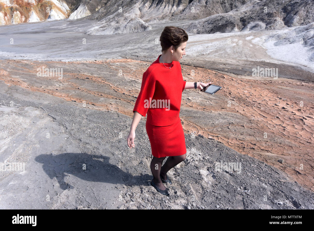 woman in a business red suit, bogged down in mud in the middle of a ...