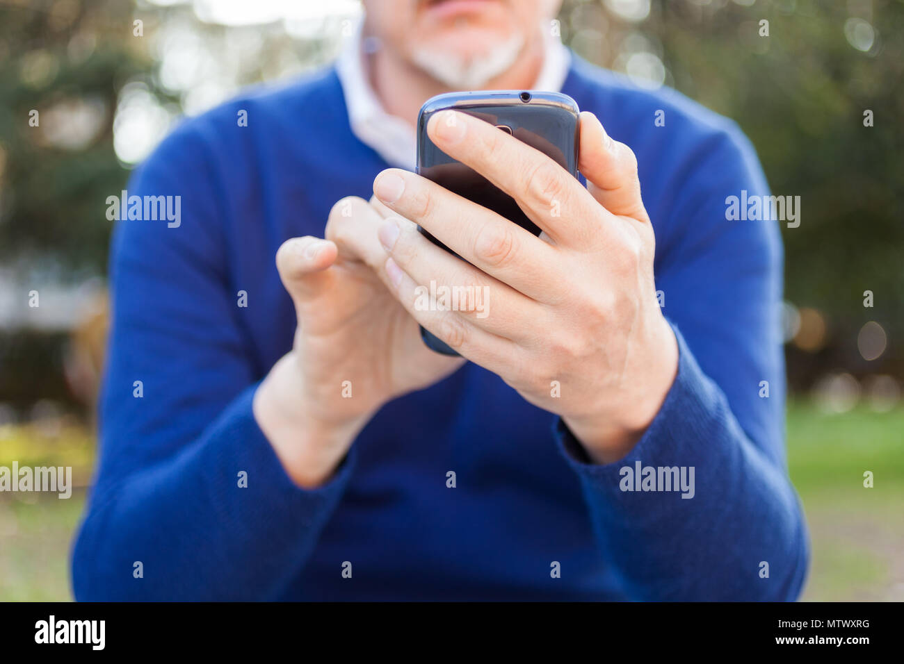 Senior man using his cell phone in a park Stock Photo - Alamy