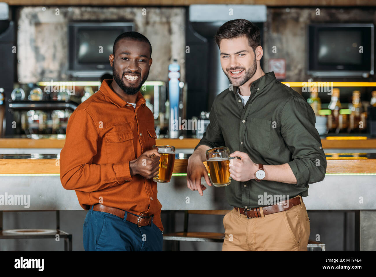 happy young men with mugs of beer at bar counter looking at camera ...