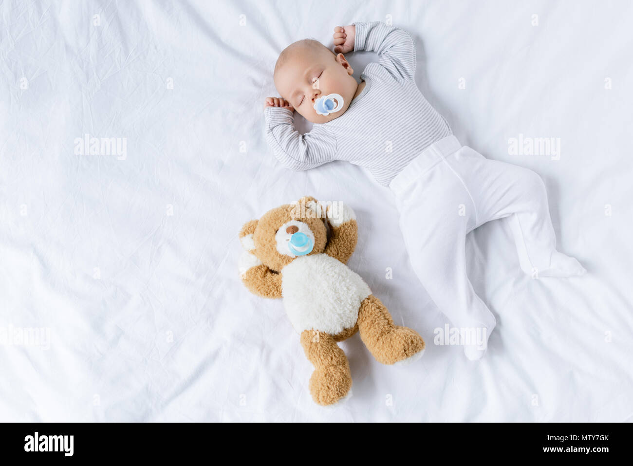 overhead view of cute baby with pacifier sleeping on bed with teddy ...