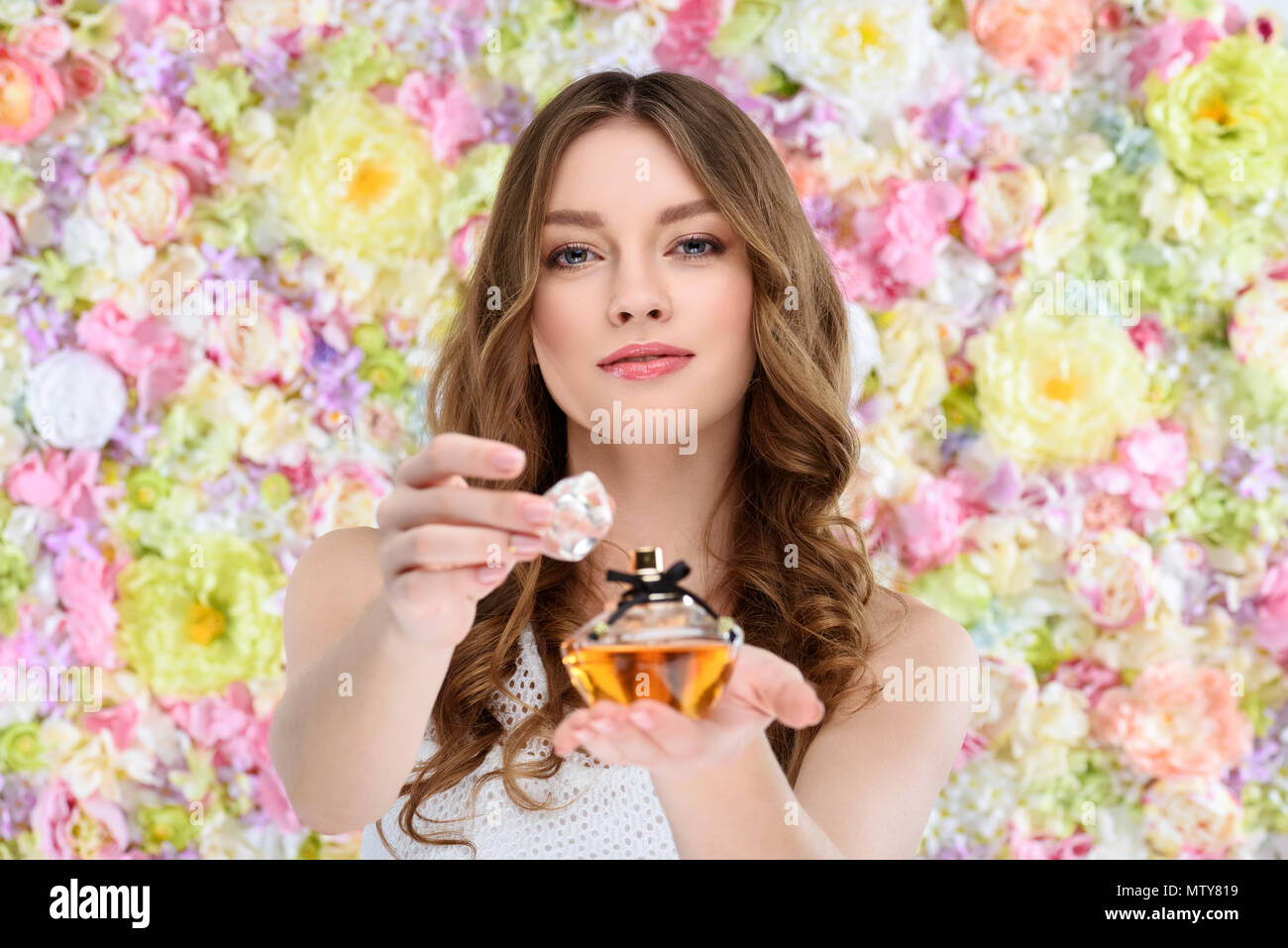 beautiful young woman opening bottle of perfume on floral background ...