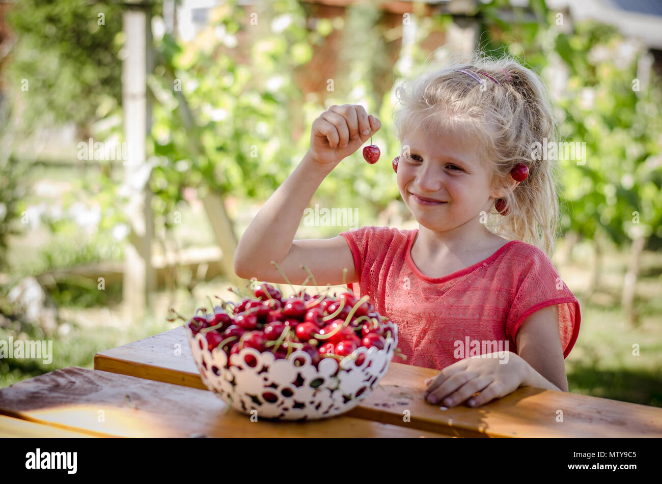 adorable blond girl eating cherry fruit in the garden Stock Photo - Alamy