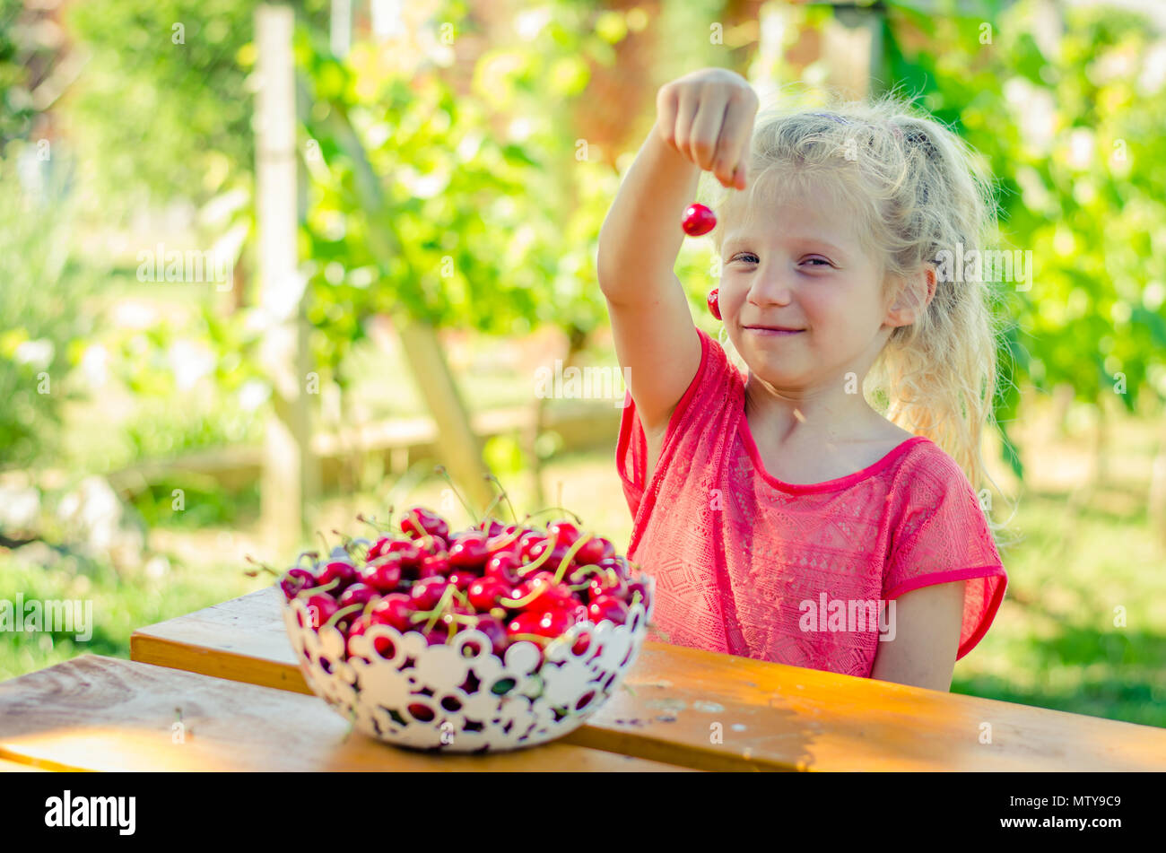 lovely blond girl eating cherry outdoors in the garden Stock Photo - Alamy
