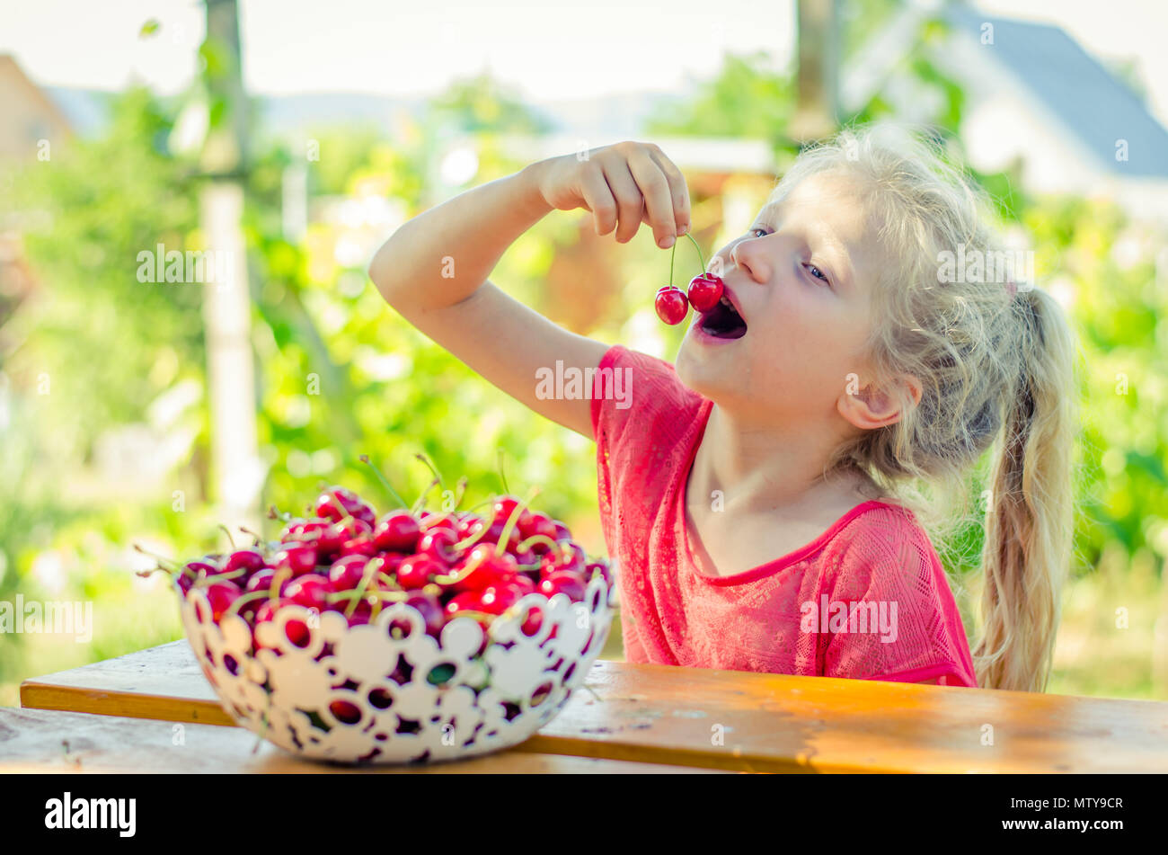 lovely blond girl eating cherry outdoors in the garden Stock Photo - Alamy